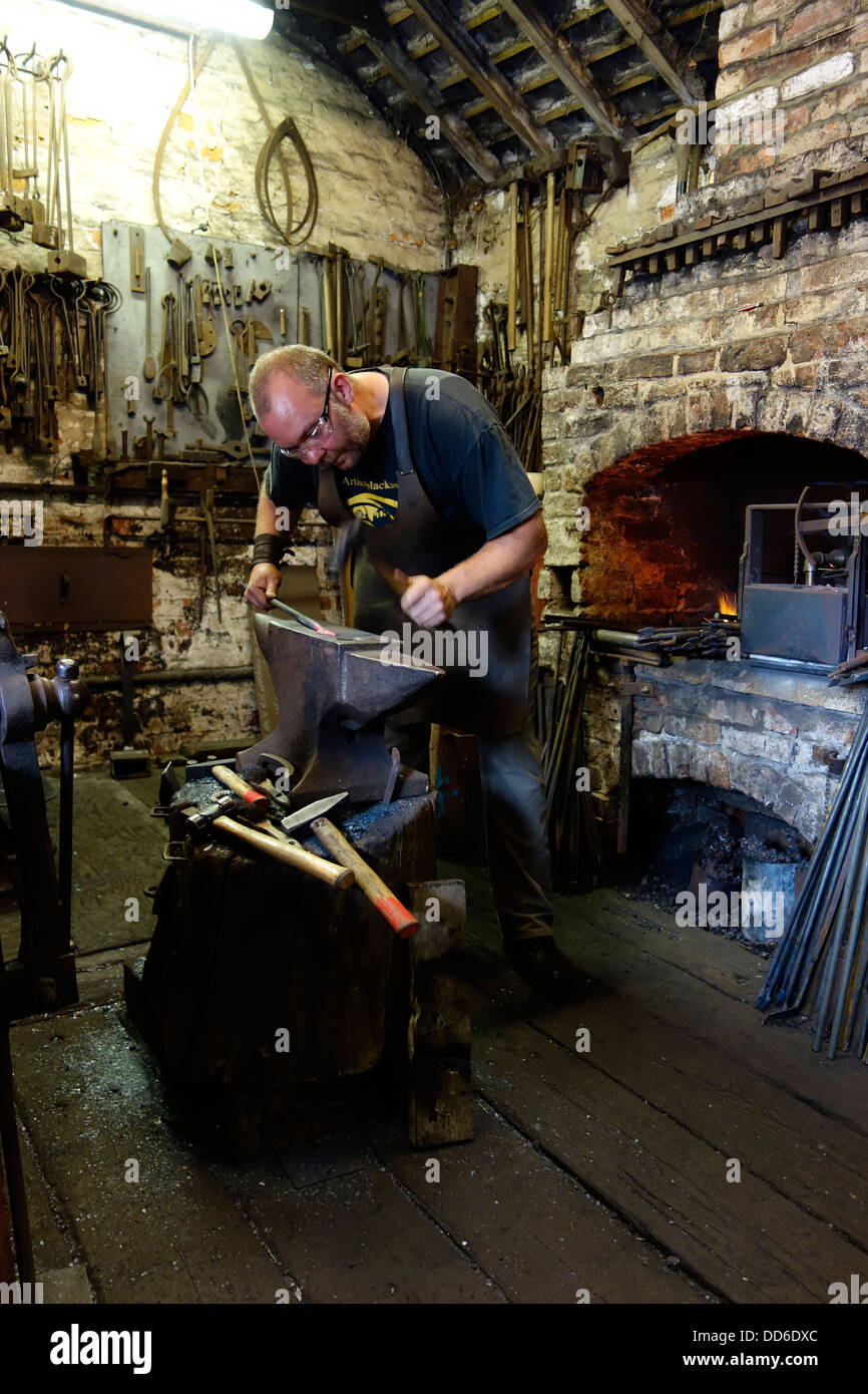 Blacksmith hammering a piece of iron on an anvil in a heritage museum ...