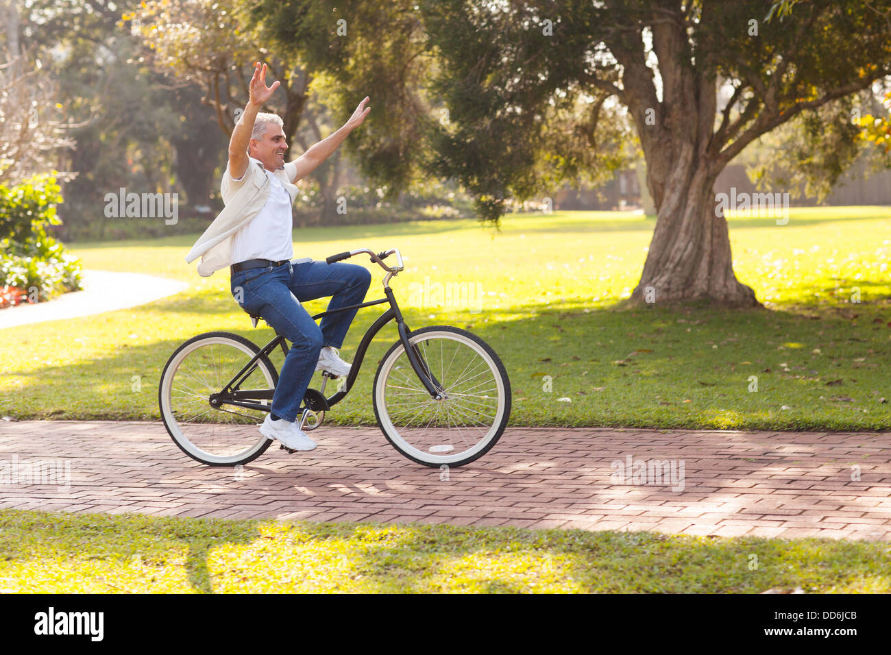 playful middle aged man riding a bike outdoors with arms up Stock Photo ...