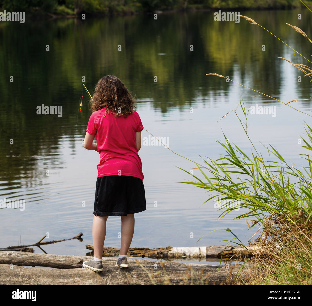 Photo of young girl, back to camera, scanning lake before casting with ...