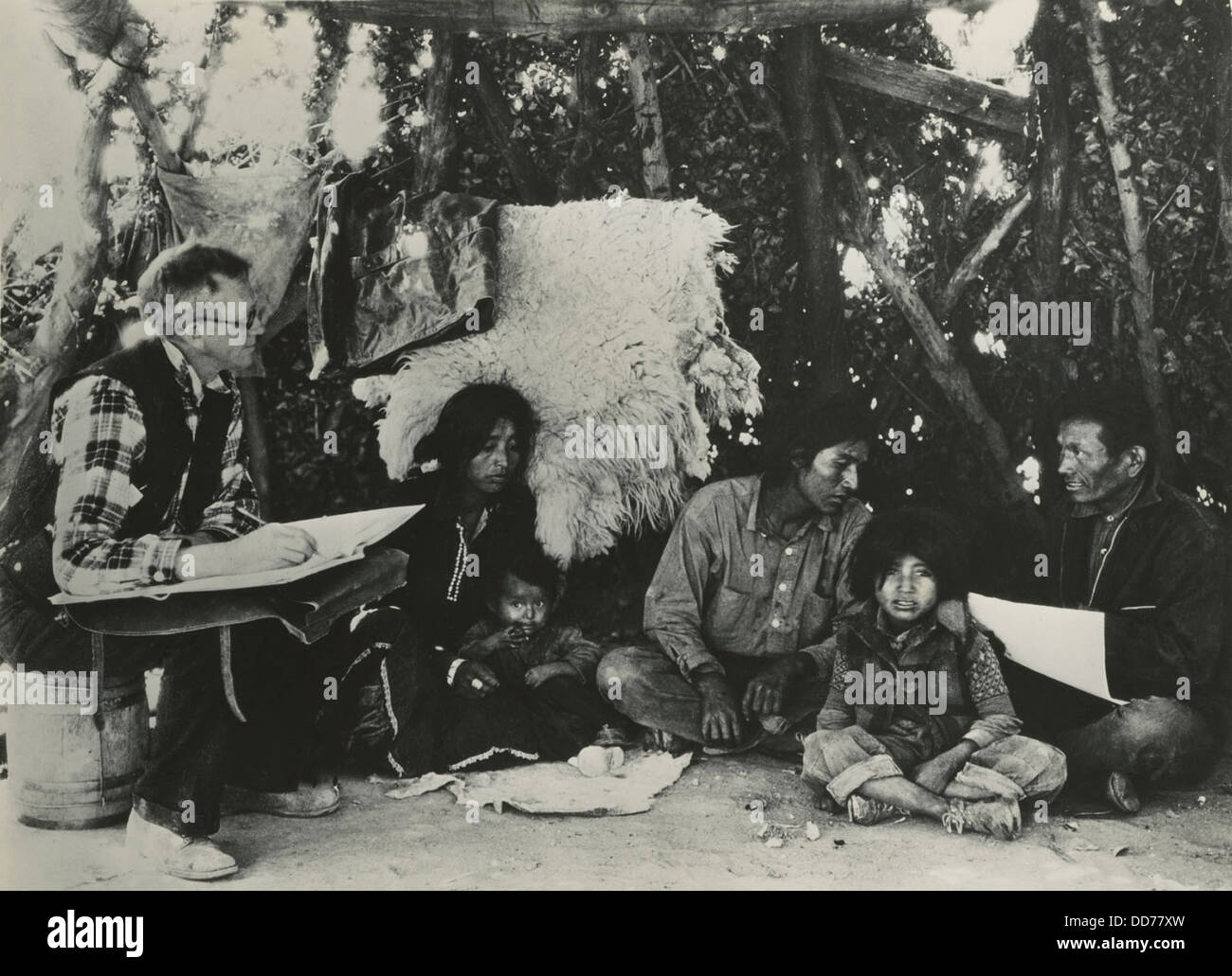 1940 Census taker, seated on a barrel, interviewing a Navajo family. At ...