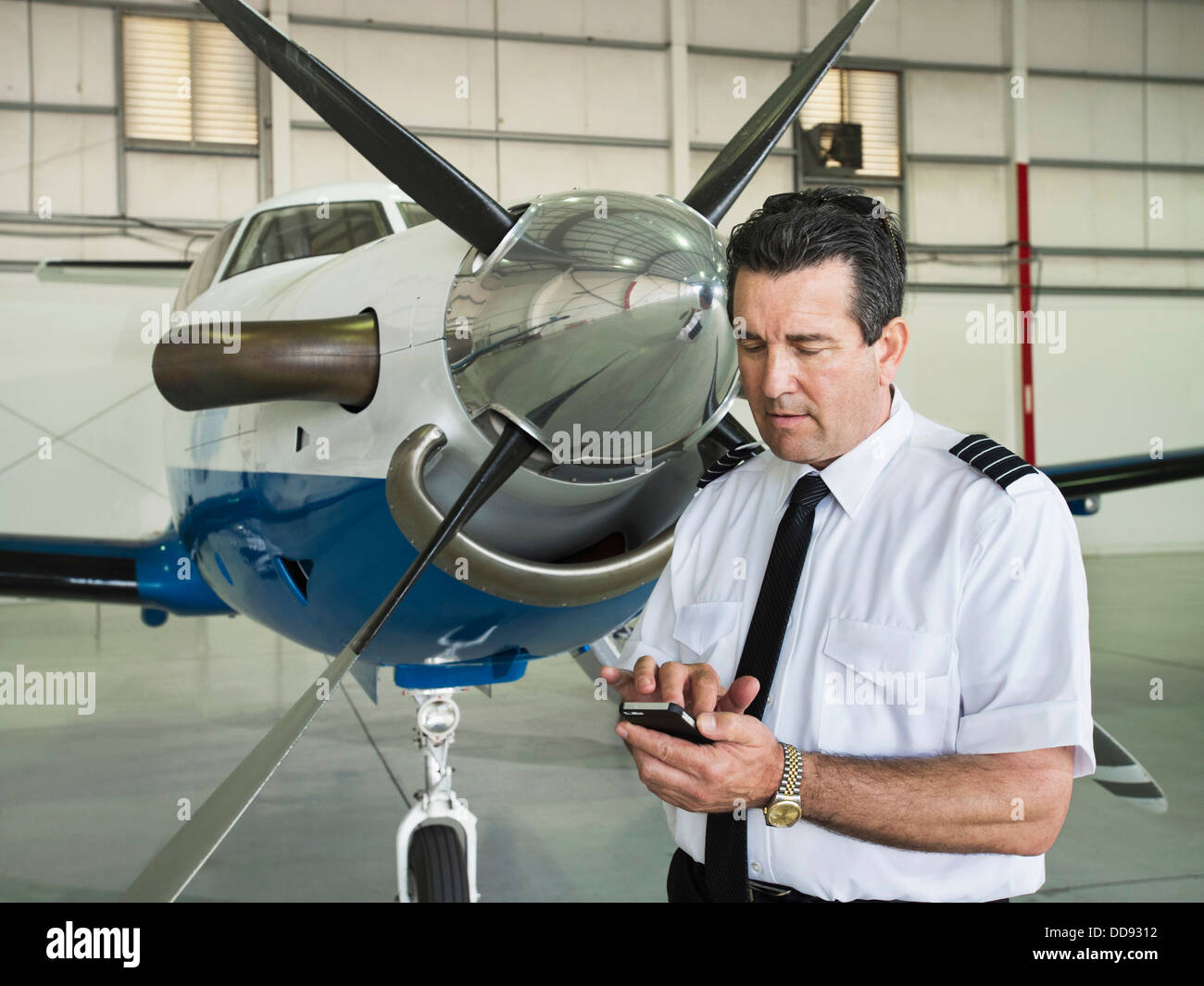 Caucasian pilot using cell phone in hangar Stock Photo - Alamy