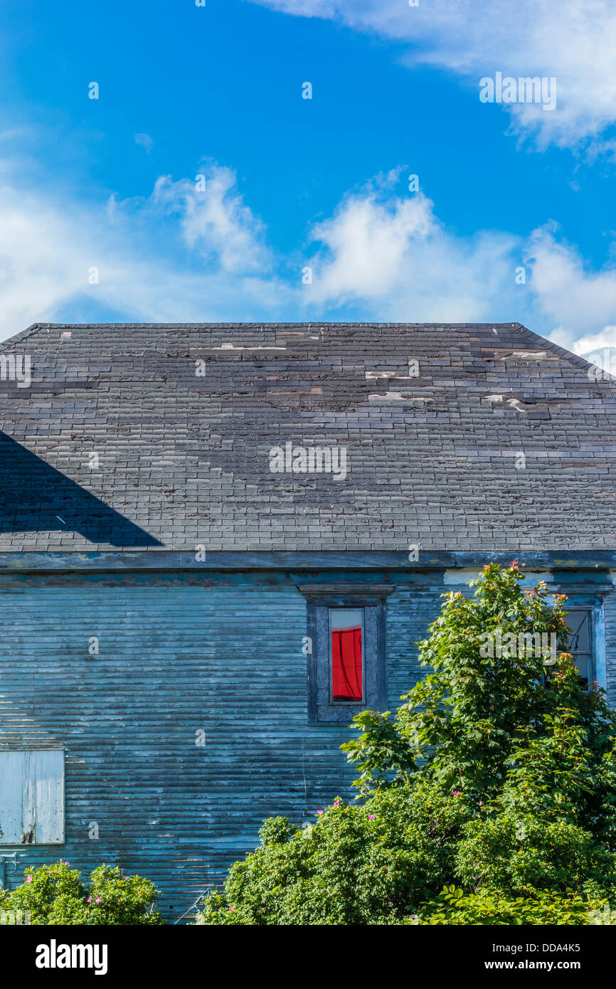 A red reflection of a red metal roof in a window of a deserted, run ...