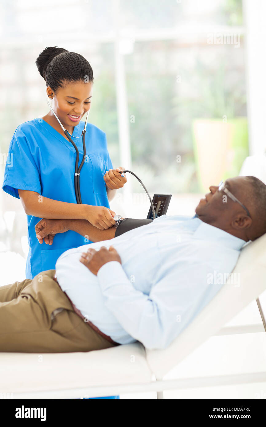 friendly young African doctor checking senior patient's blood pressure ...