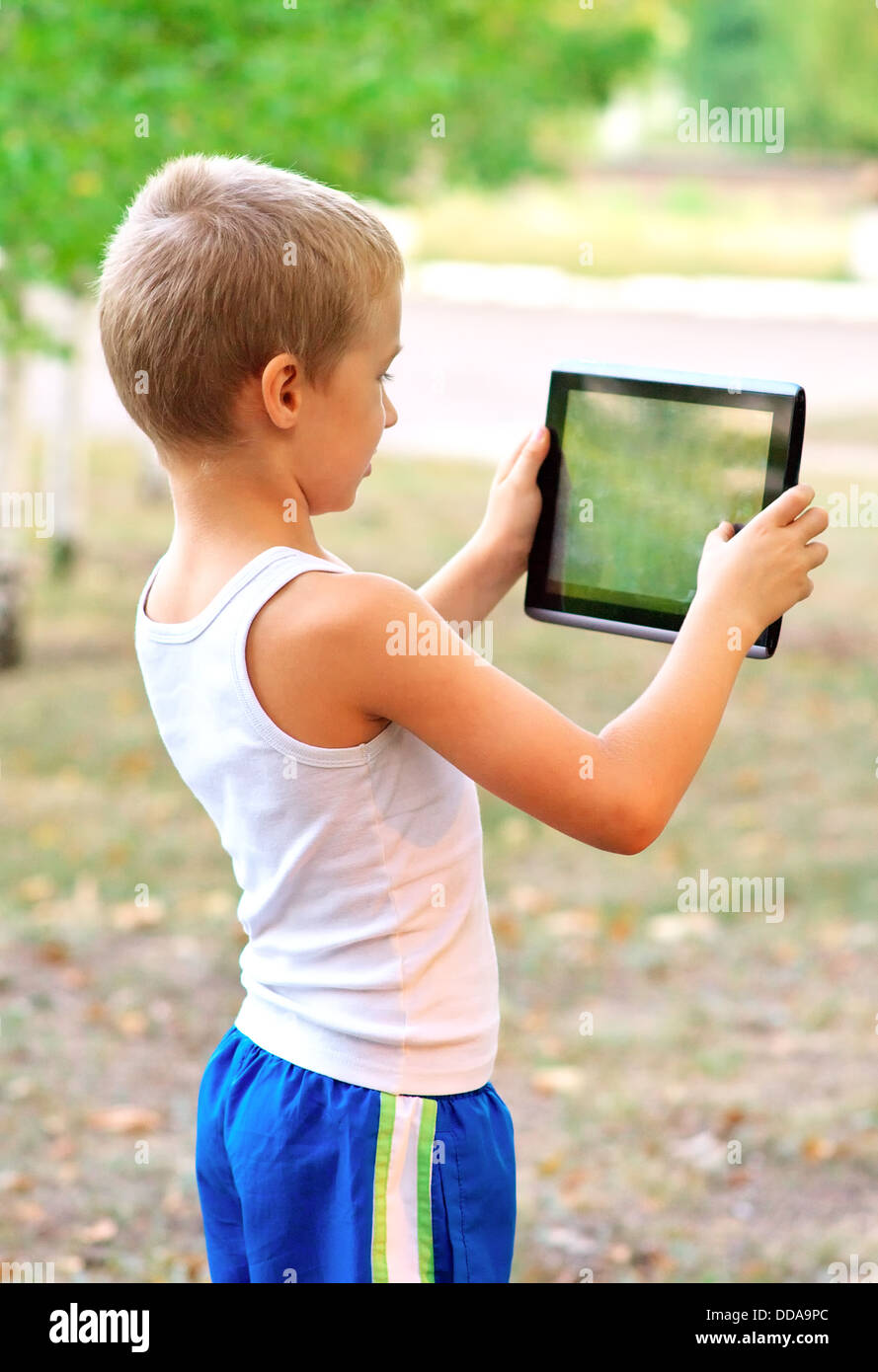 Boy Child playing with Tablet PC standing Outdoor with nature on ...