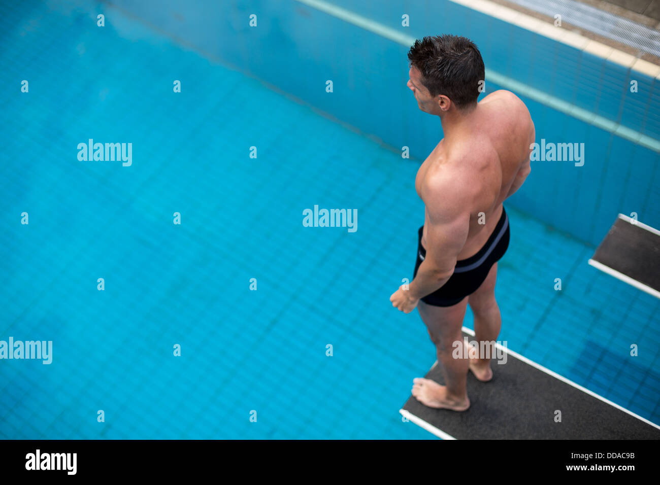 Man standing on diving board at public swimming pool above the water ...