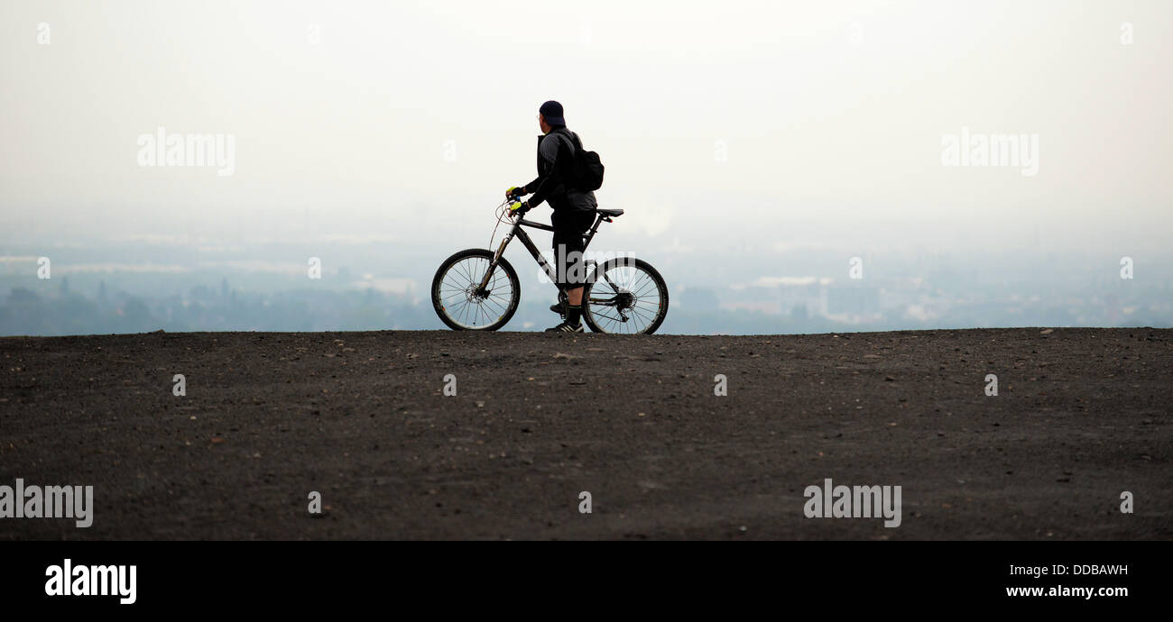 A cyclist looks into the distance as he stands with his bicycle on an ...