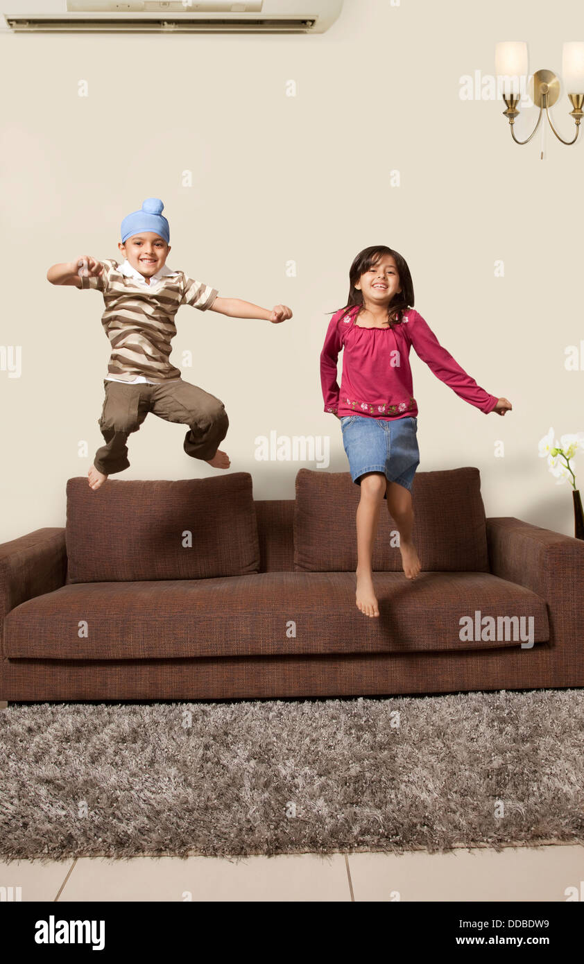 Happy brother and sister jumping on sofa at home Stock Photo - Alamy
