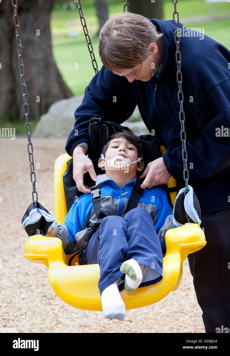 Father pushing disabled son on handicap swing Stock Photo - Alamy