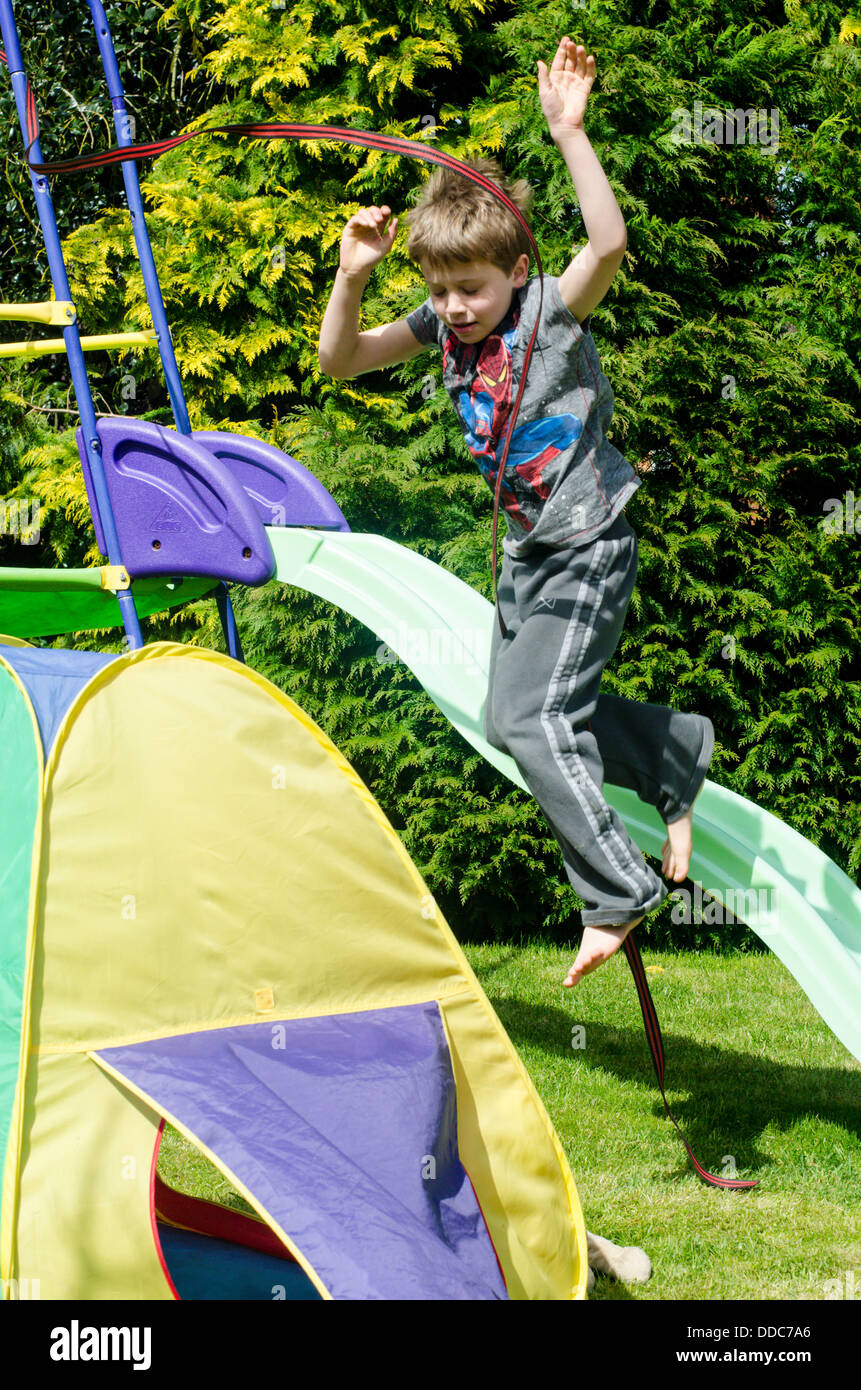 eight year old boy jumping from a climbing frame slide in garden onto a ...