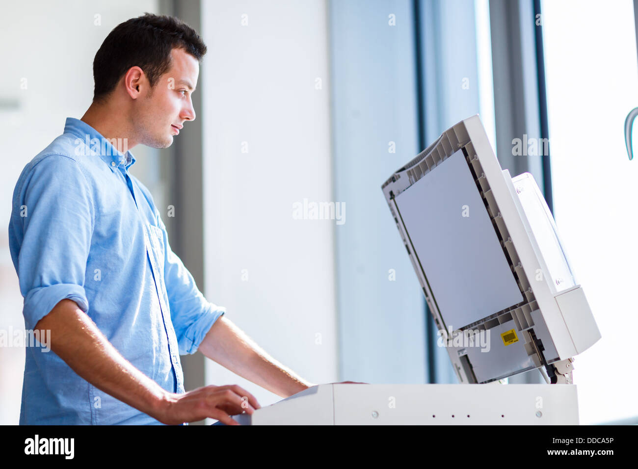 Handsome young man using a copy machine Stock Photo - Alamy