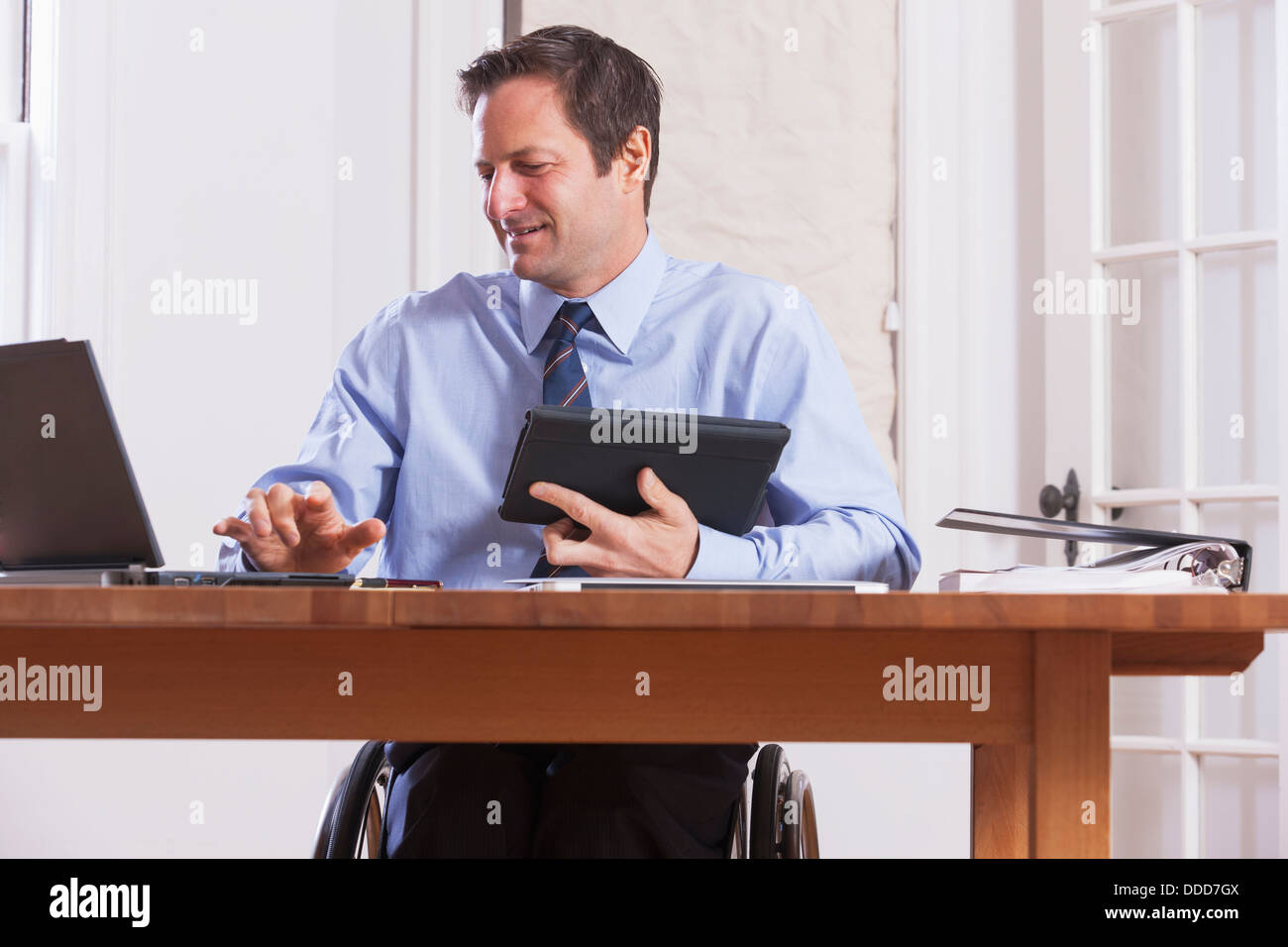 Businessman with spinal cord injury in a wheelchair using a tablet and ...