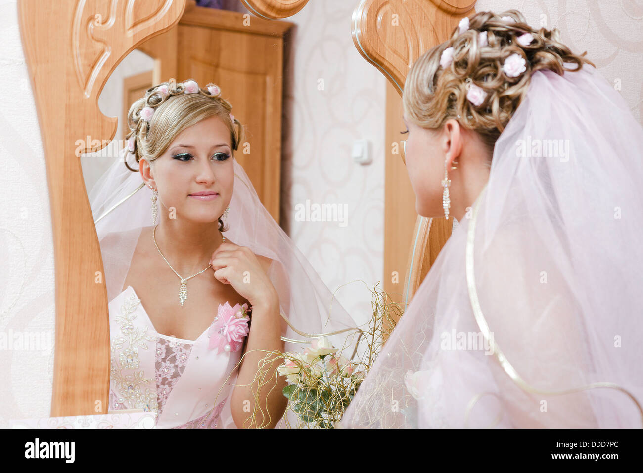 Beautiful bride in a pink dress looks in the mirror Stock Photo - Alamy