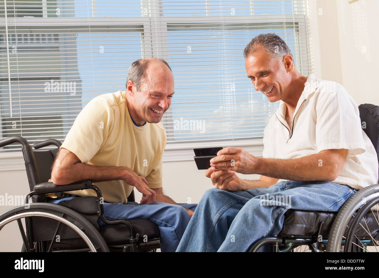 Two disabled men sitting in wheelchairs using a smart phone Stock Photo ...