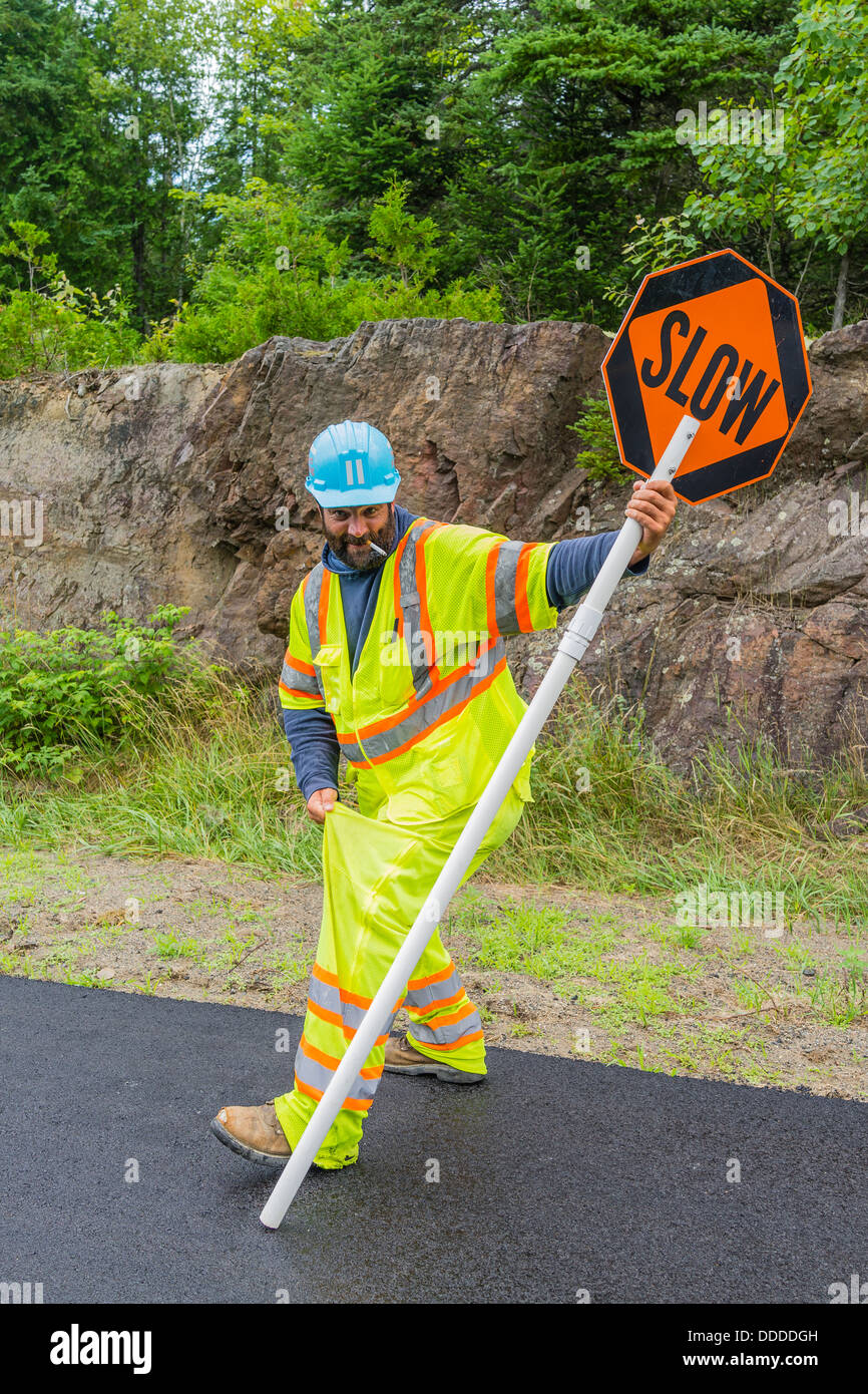 A flagman, dressed in bright yellow-green clothing holds a traffic sign ...