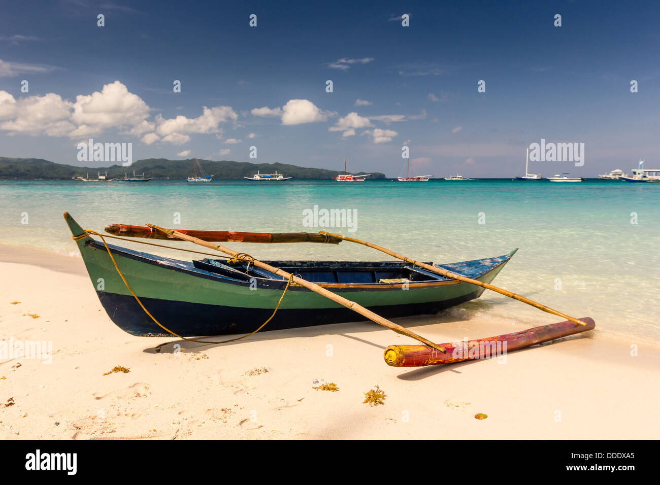 A small wooden traditional boat on a tropical beach next to calm, clear ...