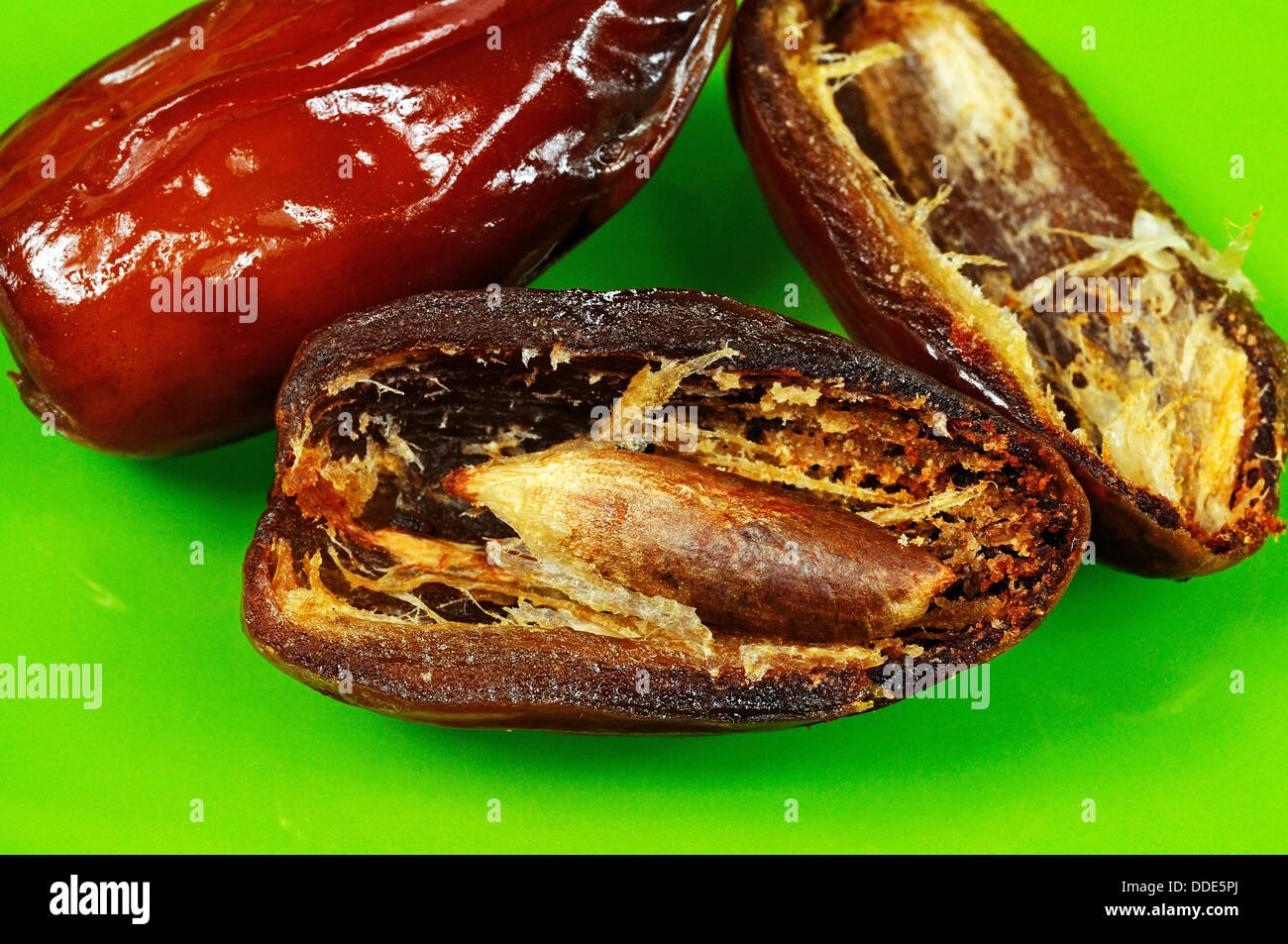 Dates, one whole, one halved against a green background Stock Photo - Alamy
