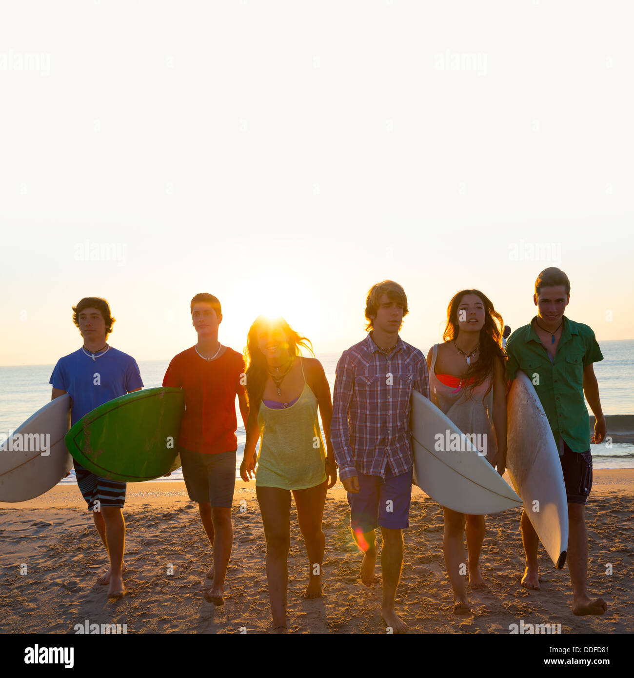 Surfers teen boys and girls group walking on beach at sunshine sunset ...
