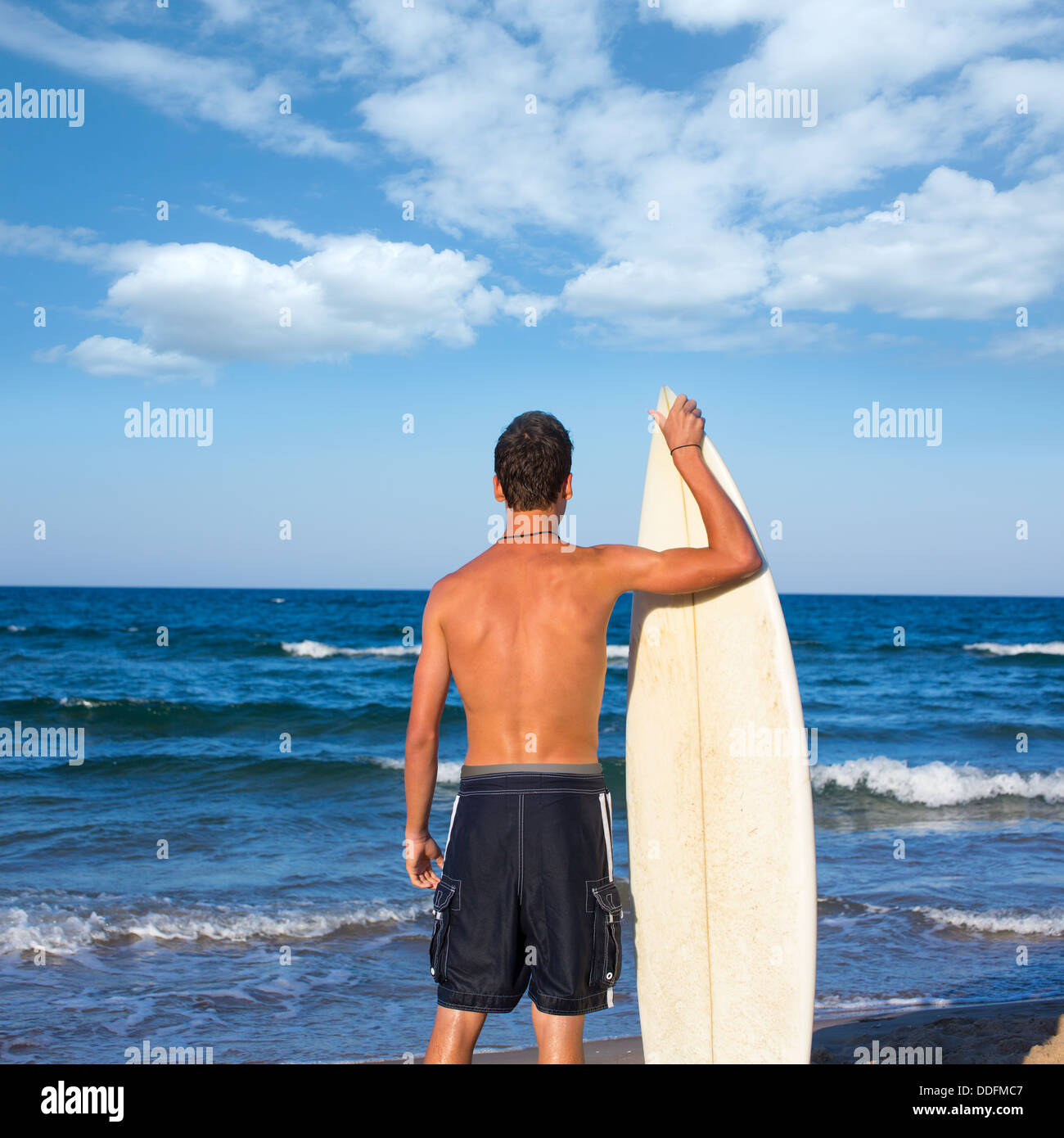 Boy surfer back rear view holding surfboard on blue beach Stock Photo ...