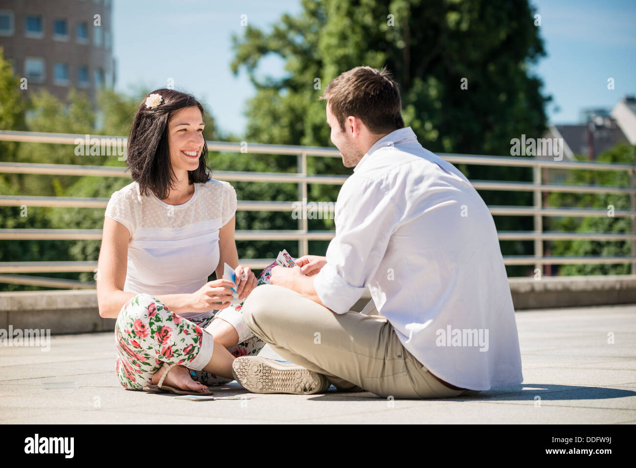 Young couple playing cards outdoor sitting on ground Stock Photo - Alamy