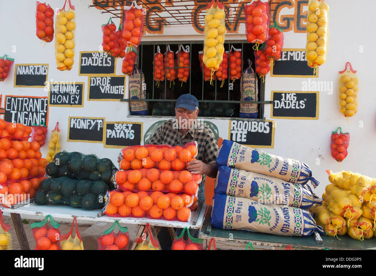 Farmer selling oranges and other farm produce in front of a farm-stall ...