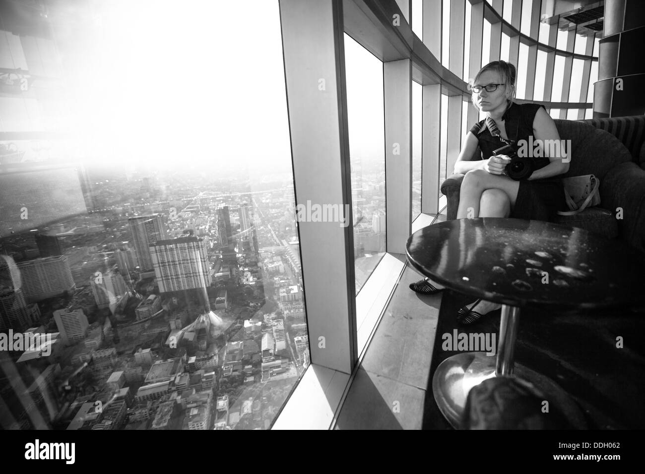 A young woman sitting by the window at skyscraper, black and white ...