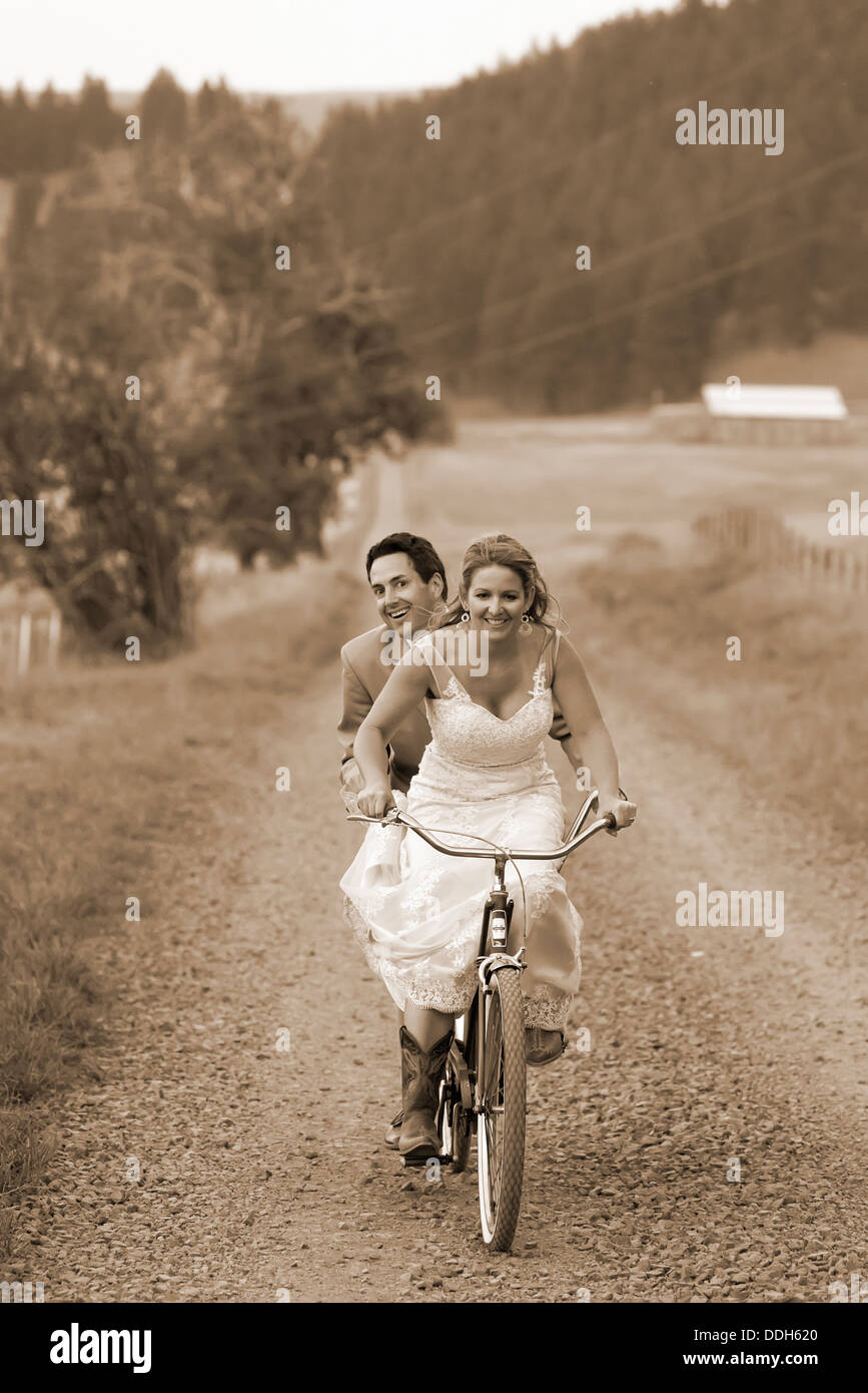 Bride and groom riding a tandem bicycle on their wedding day in Oregon ...