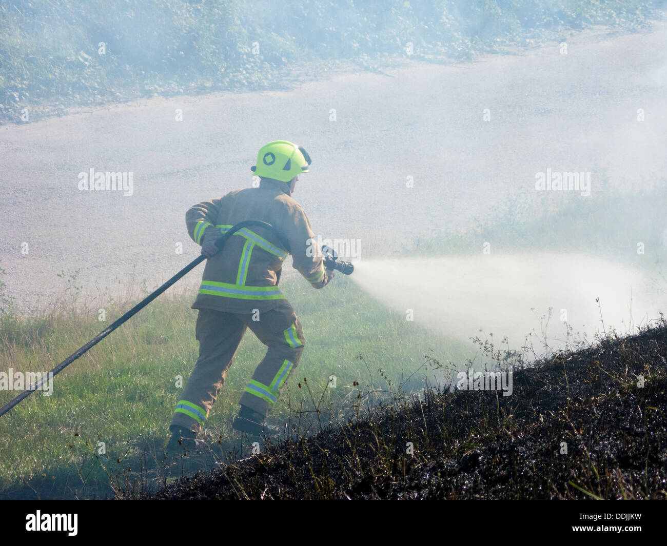 Fireman dousing down a grass fire, Kent, UK, summer Stock Photo - Alamy