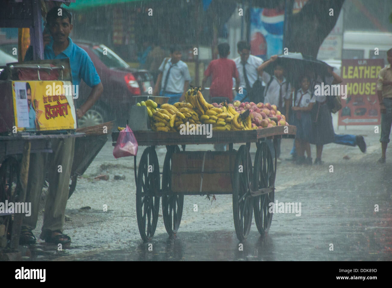 Fruit cart in heavy rain with children sheltering in background under ...