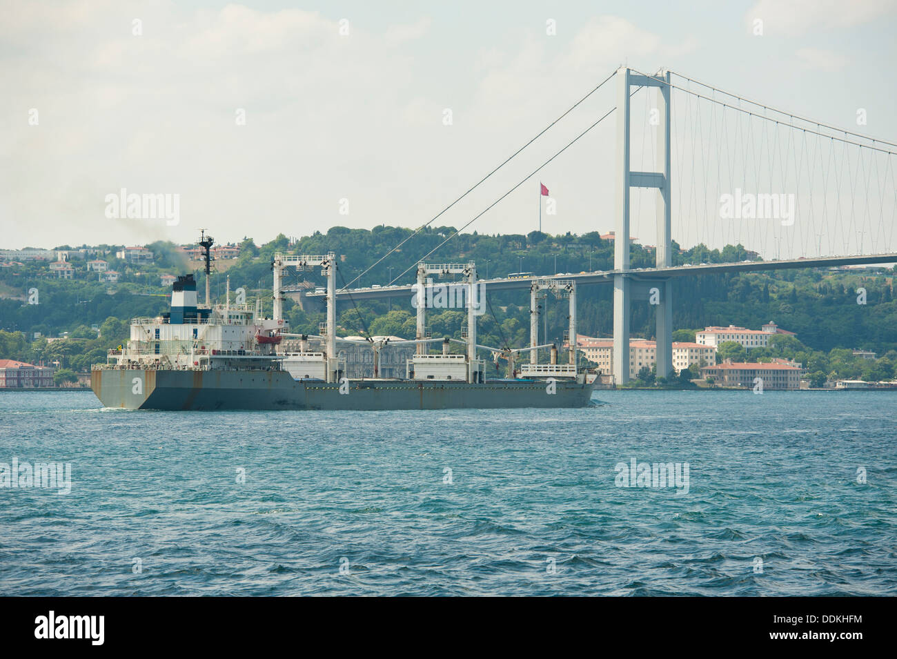Large cargo ship traveling under a suspension bridge on bosphorus river ...