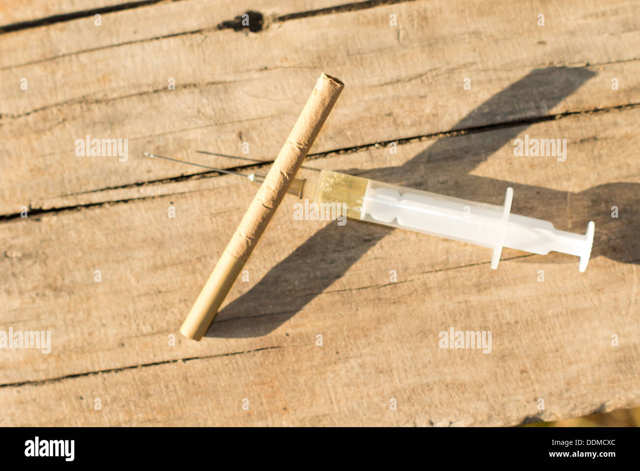 Close-up of a brown cigarette and a syringe filled with a dose of ...