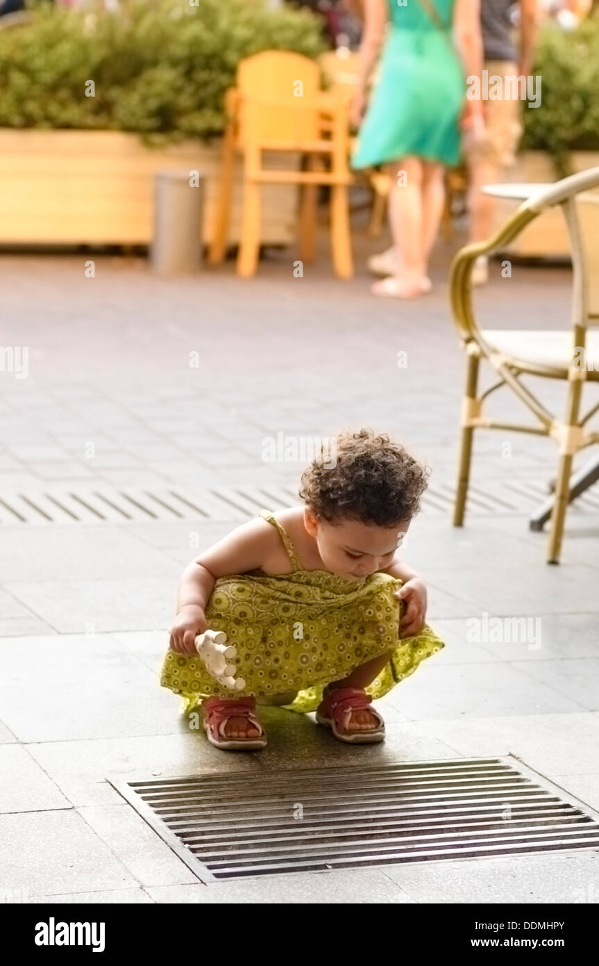Toddler is crouching on the pavement looking at air duct Stock Photo ...