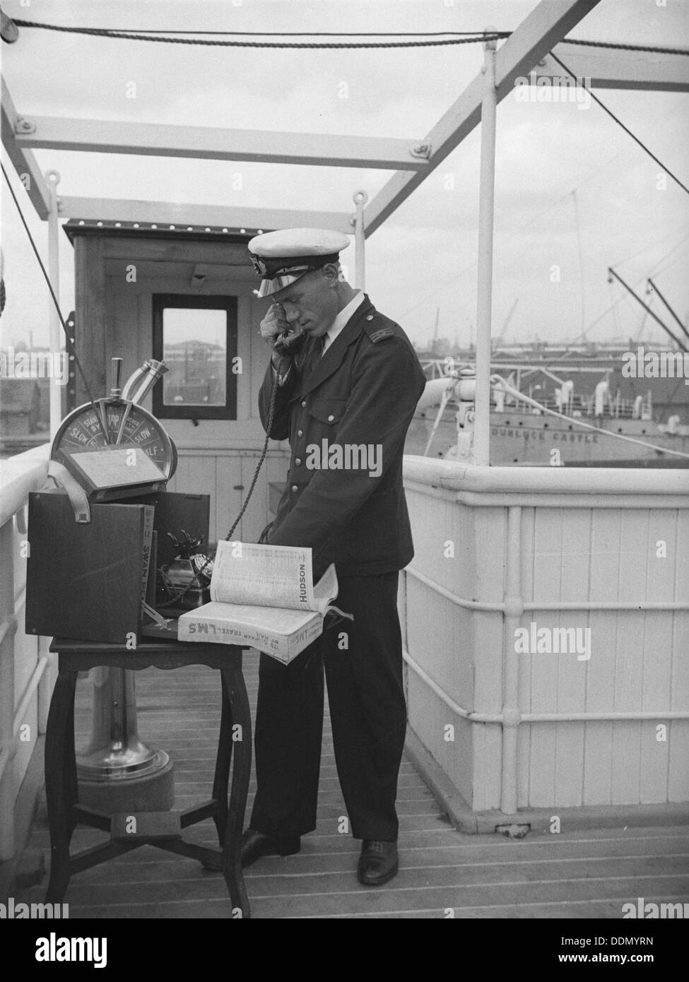 A ship's officer on the bridge uses a portable telephone connected to a ...