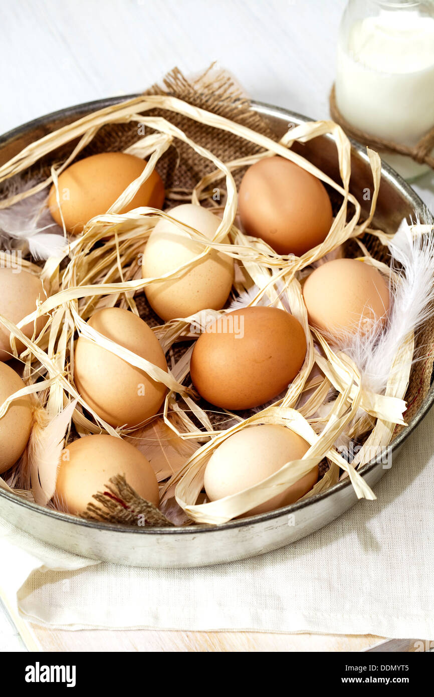 A shallow metal bowl filled with fresh hen's eggs, surrounded by straw ...