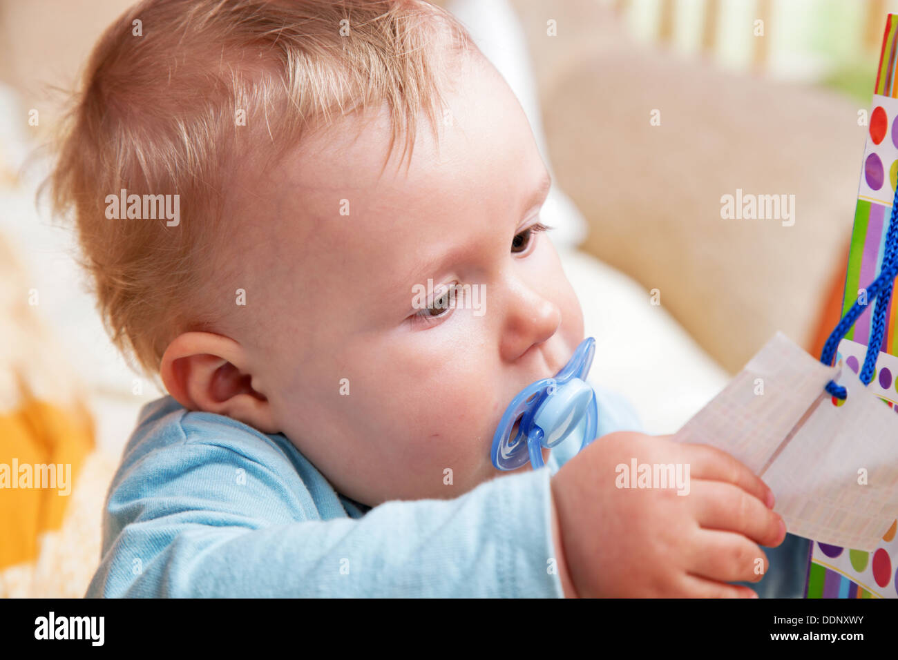 Young baby boy with a dummy in his mouth playing with colorful papers ...