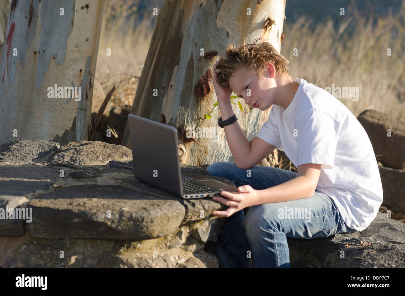 Thoughtful teenager sits on nature with laptop Stock Photo - Alamy