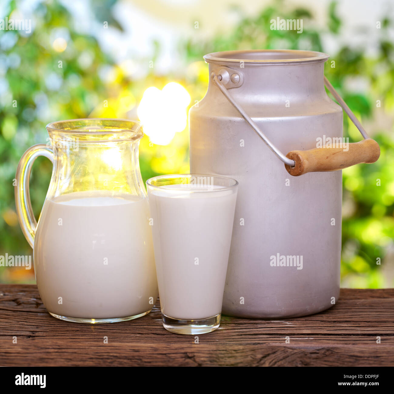 Milk in various dishes on the old wooden table in an outdoor setting ...