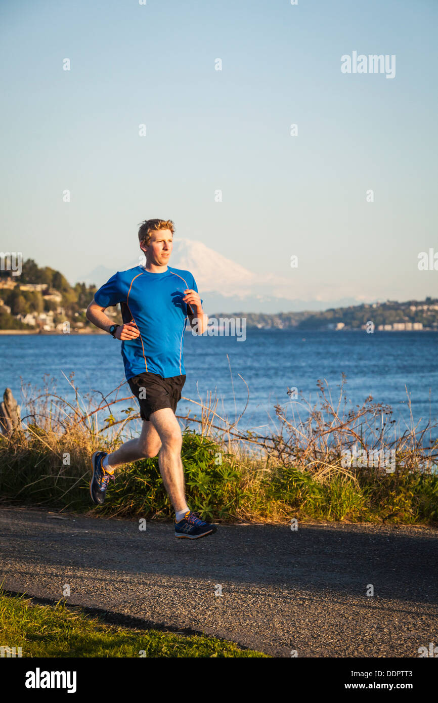 A young man running on a paved path along the water in Discovery Park ...