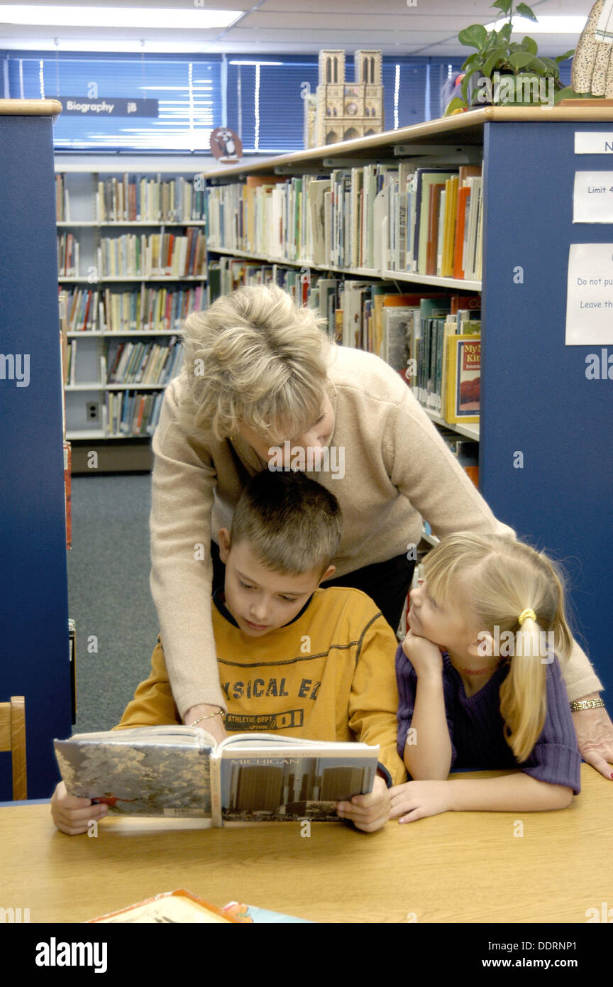 Adult woman with grandchildren reading at a library Stock Photo - Alamy