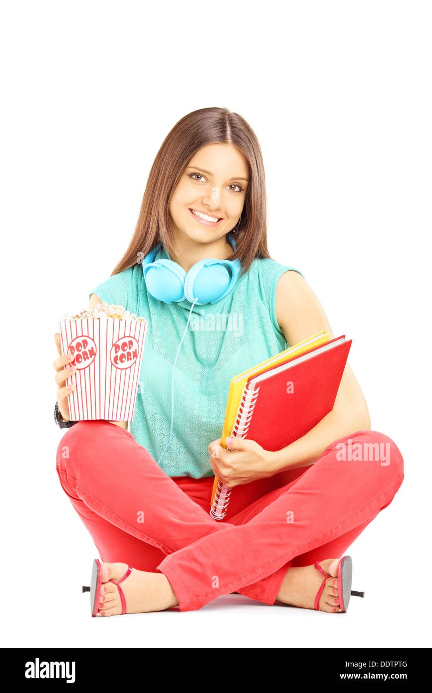 Smiling student sitting on a floor and holding notebooks and popcorn ...