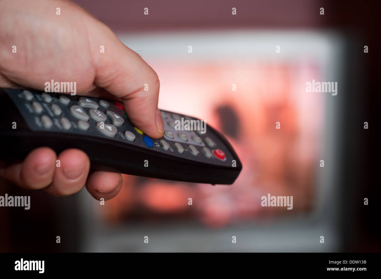 Hand holding TV remote control with a television in the background ...