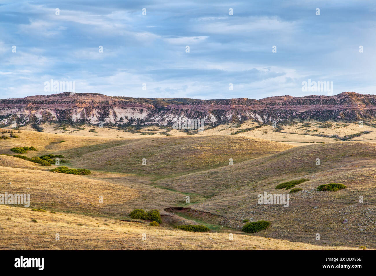 rolling prairie and cliff illuminated by sunrise at Soapstone Prairie ...