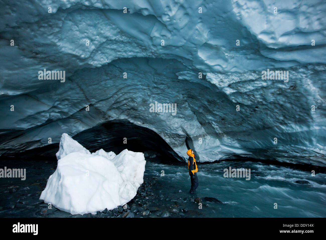 Mountaineer looking up at the ceiling of an ice cave, glacial stream ...