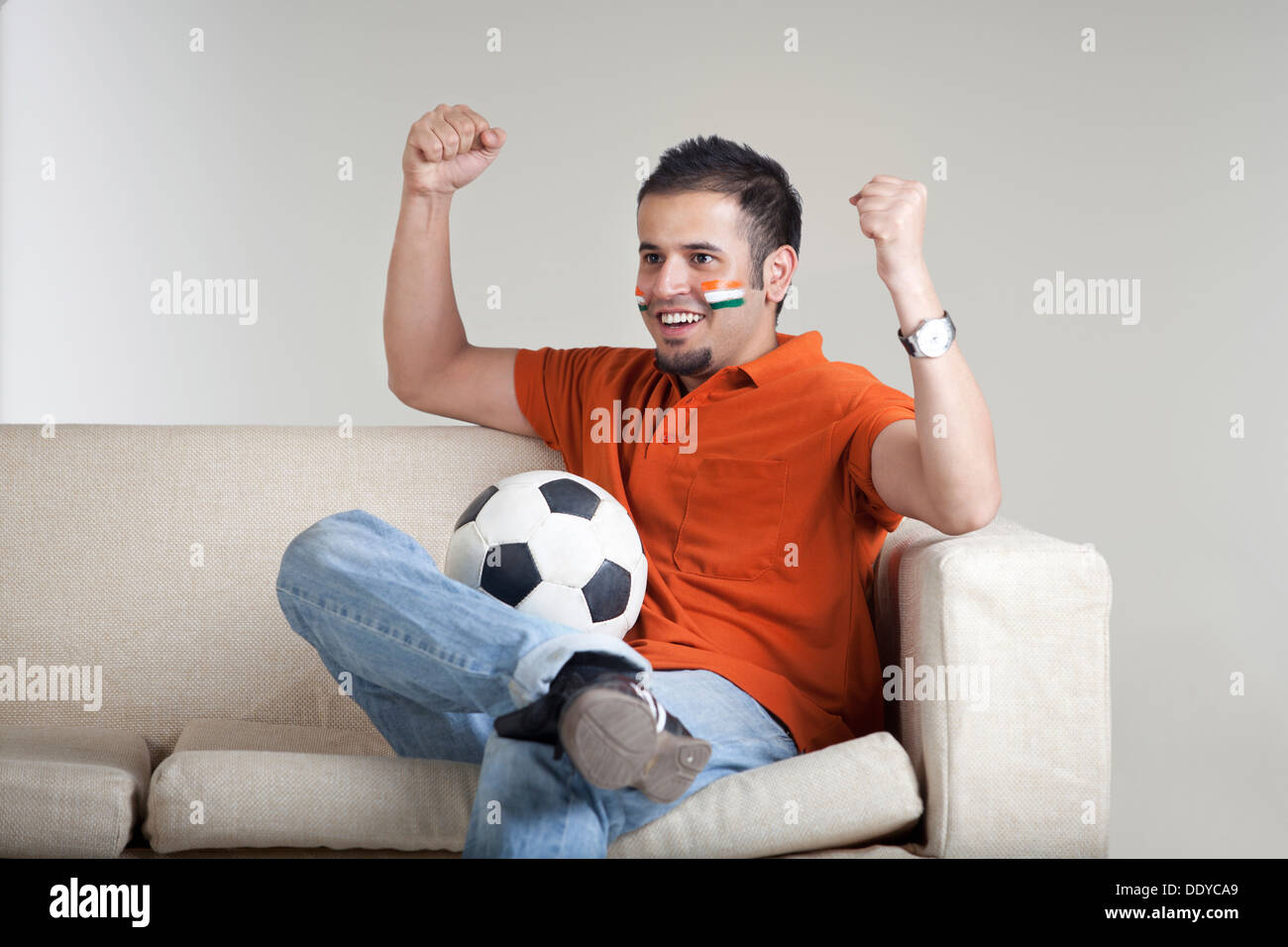 Happy young man with soccer ball cheering while sitting on sofa Stock ...
