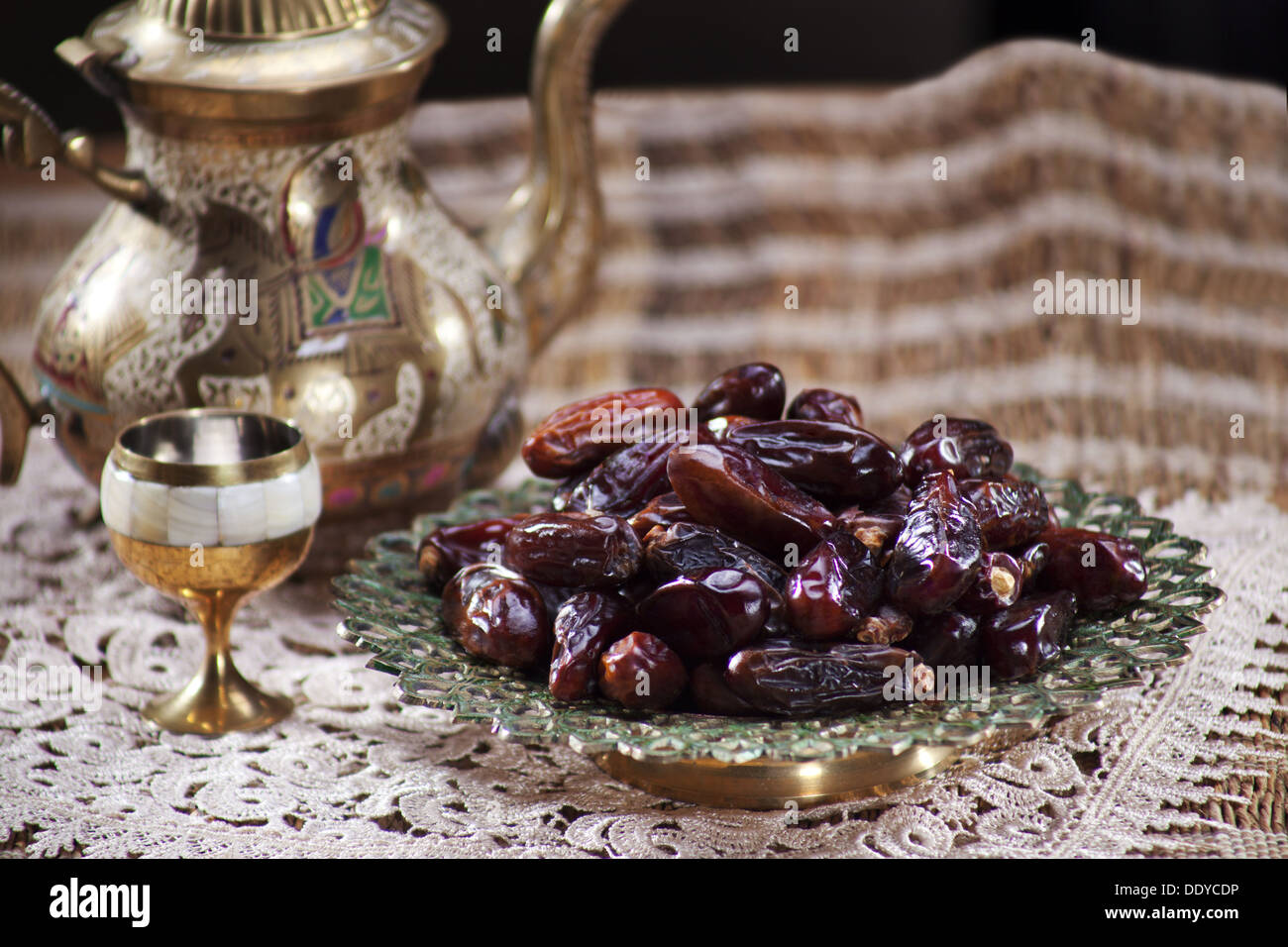 Close-up of an ornamental bowl of dried dates with kettle and glass ...