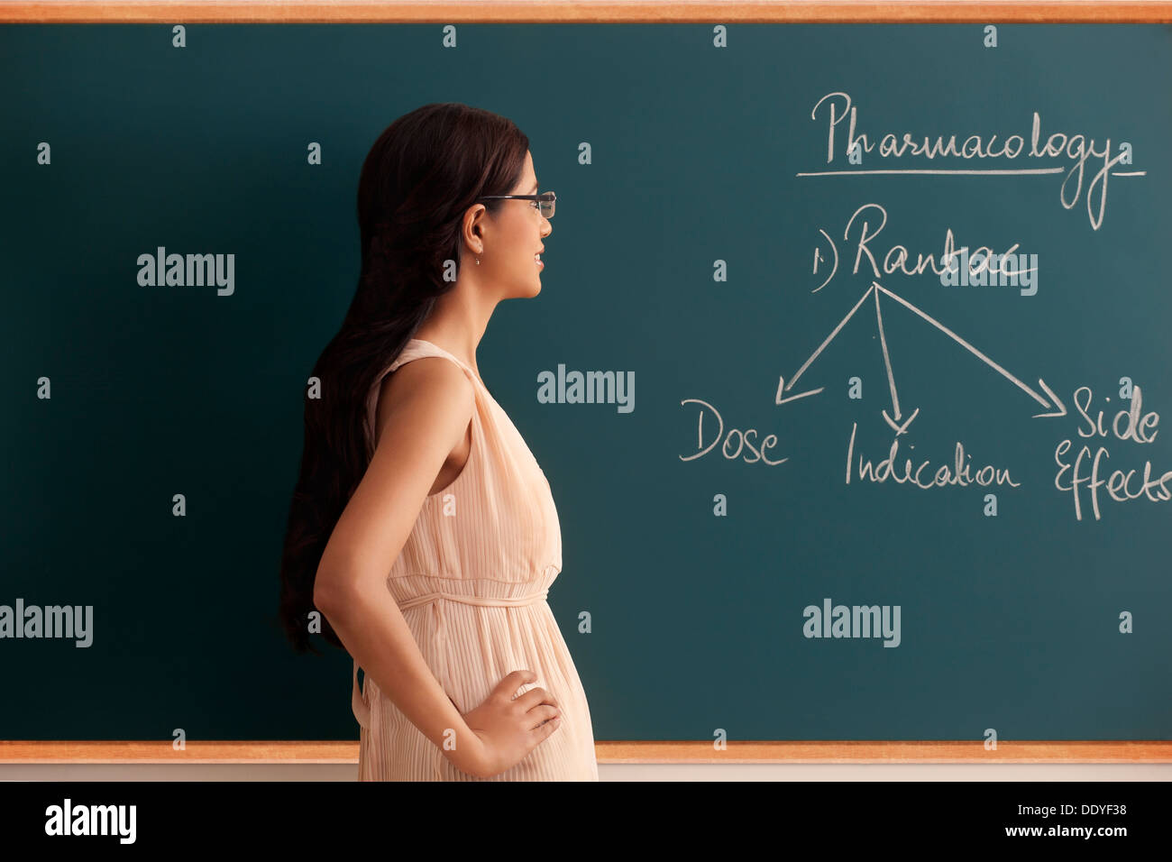 Side view of female teacher looking at written text on green board ...
