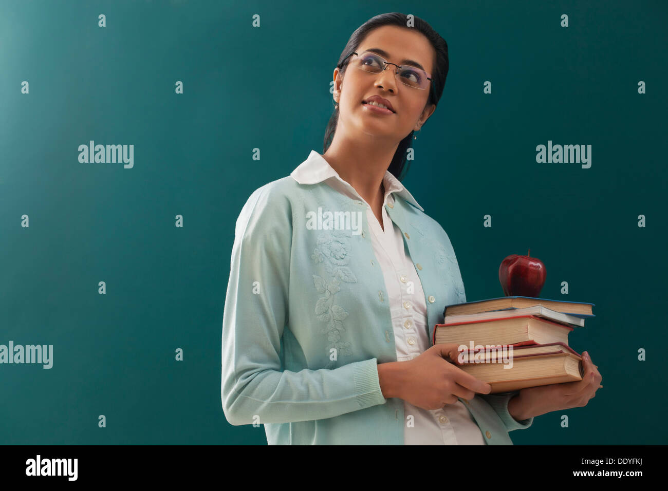Thoughtful female teacher carrying stack of books and an apple against ...