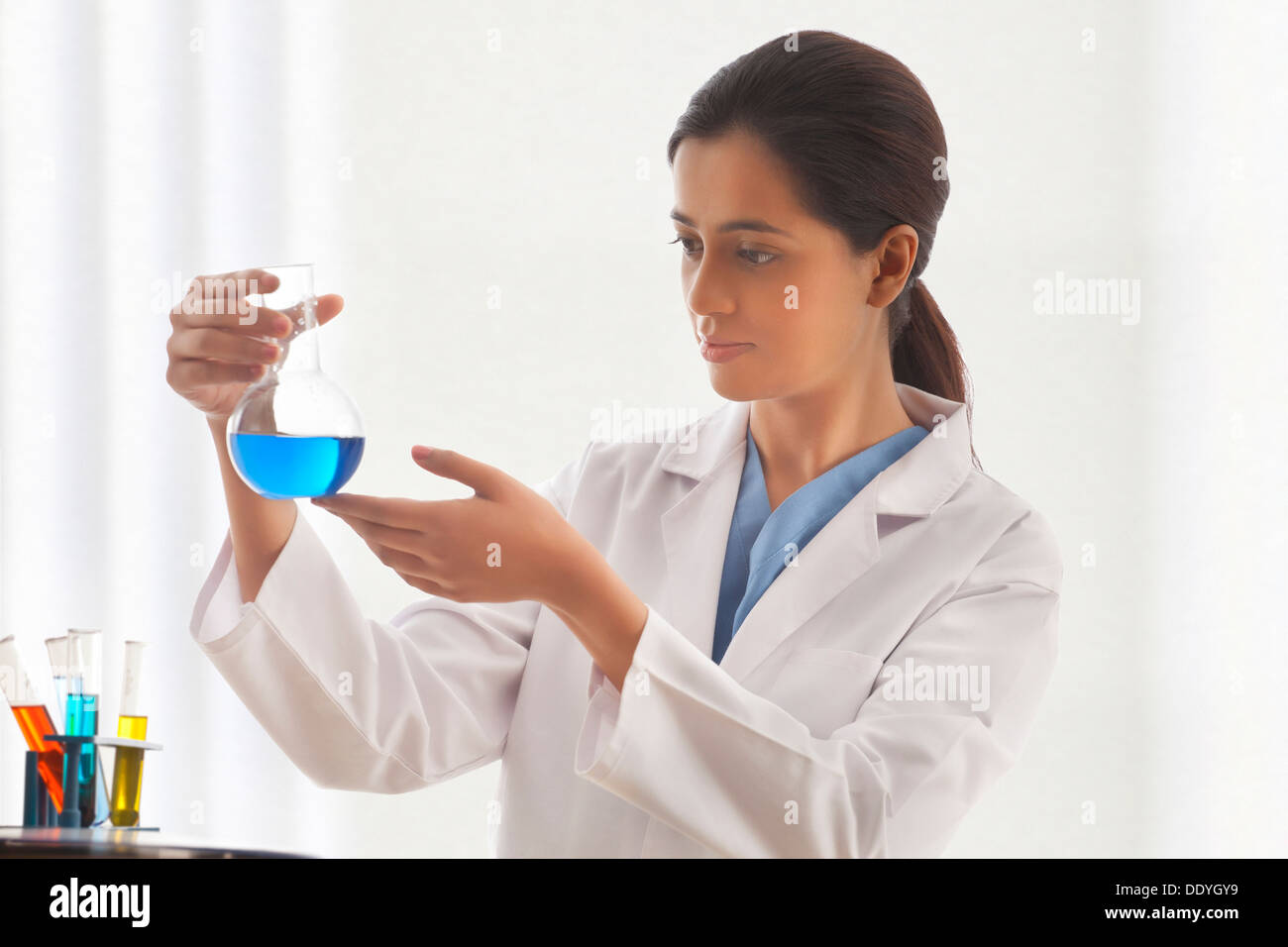 Young female scientist looking at liquid in beaker Stock Photo - Alamy