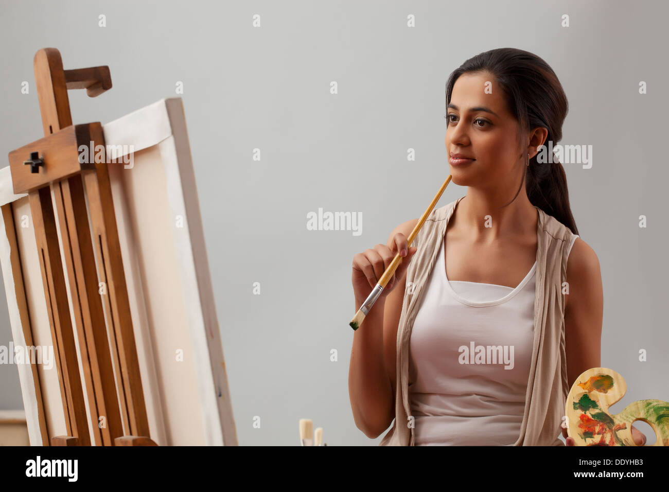 Young woman thinking while painting on canvas Stock Photo - Alamy