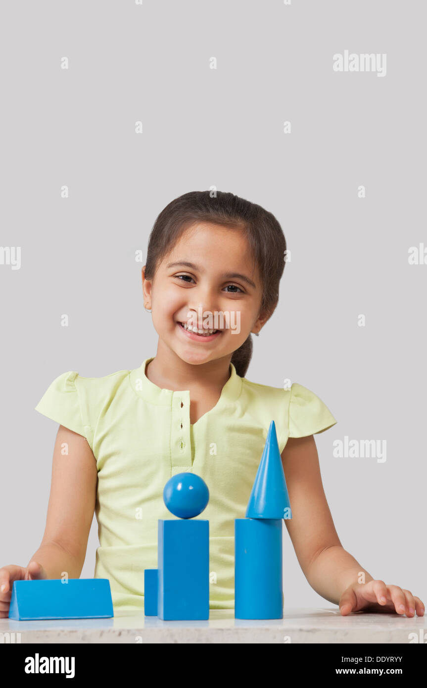 Portrait of little girl with geometry shaped blocks isolated over gray ...