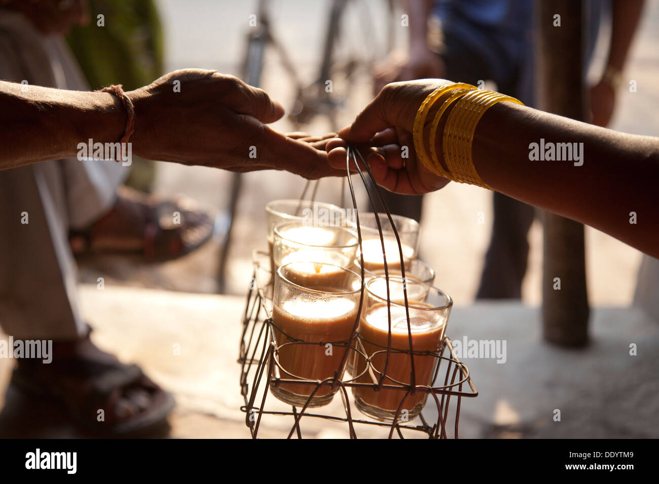 Close-up of female's hand passing tray of chai to man with people in ...
